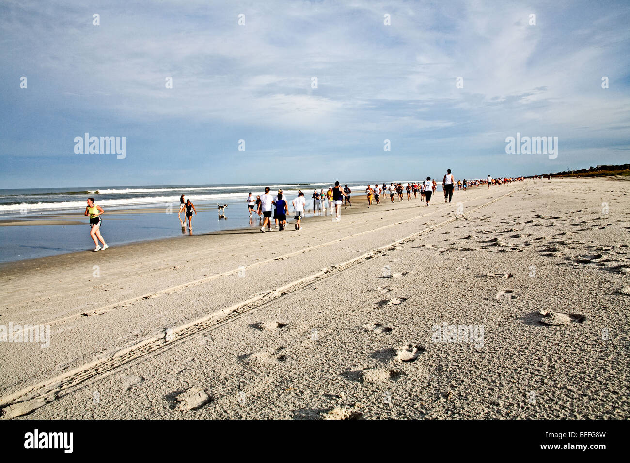 Runners running down the beach in a race by the ocean on the sand in ...