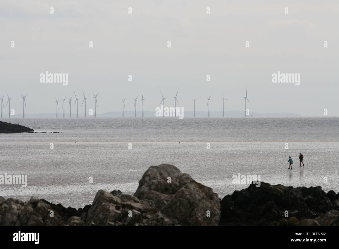 two people walking at low tide with Robin Rigg offshore wind farm in ...