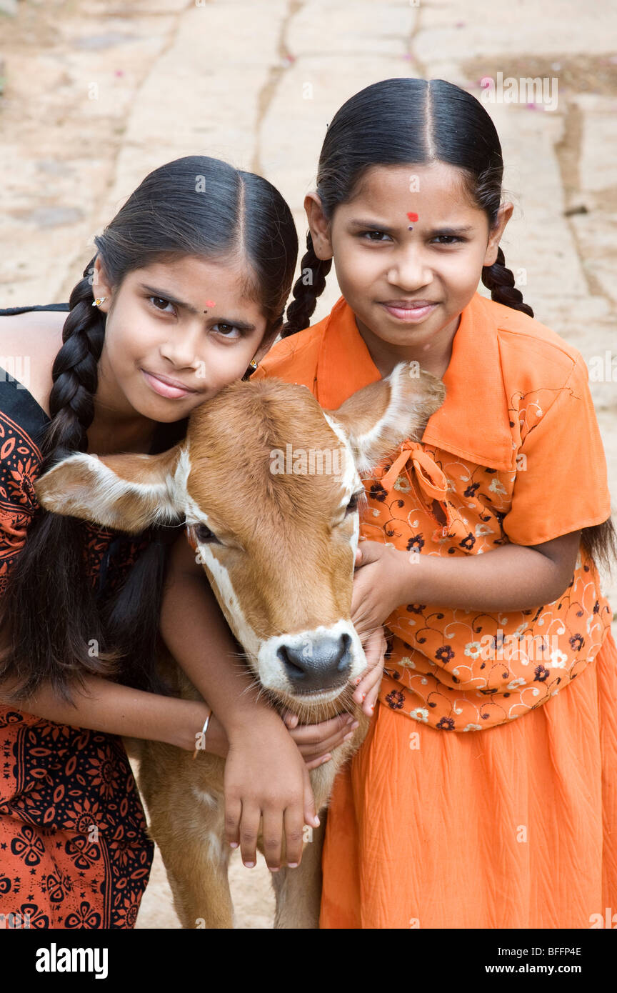 Two young Indian girls hugging a calf in a rural Indian village. Andhra ...
