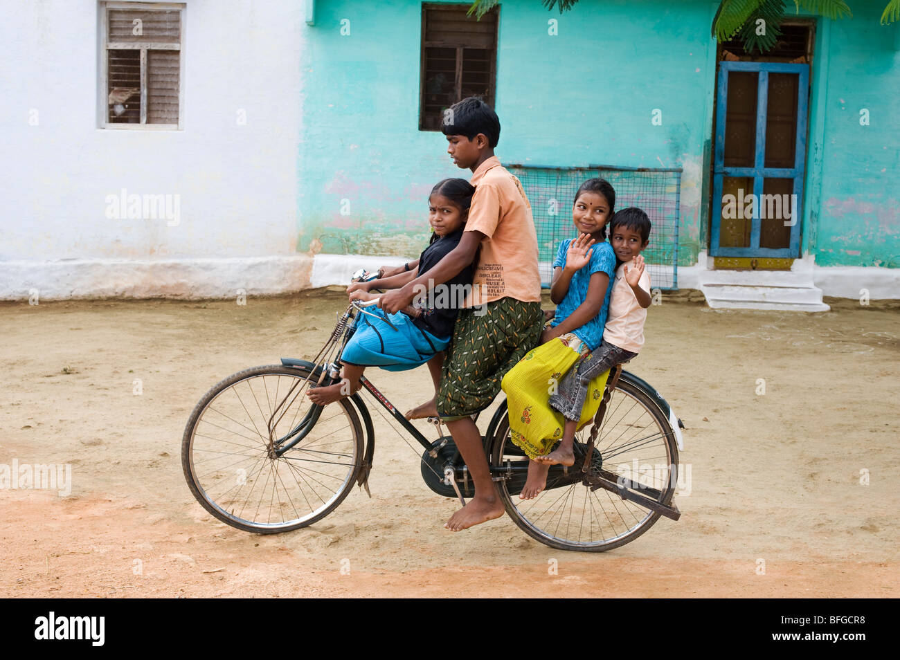 Indian teenager and children riding a bicycle in a rural Indian village ...