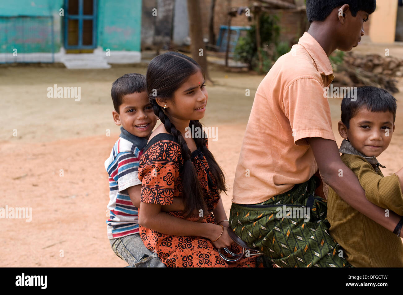 Indian teenager and children riding a bicycle in a rural Indian village ...