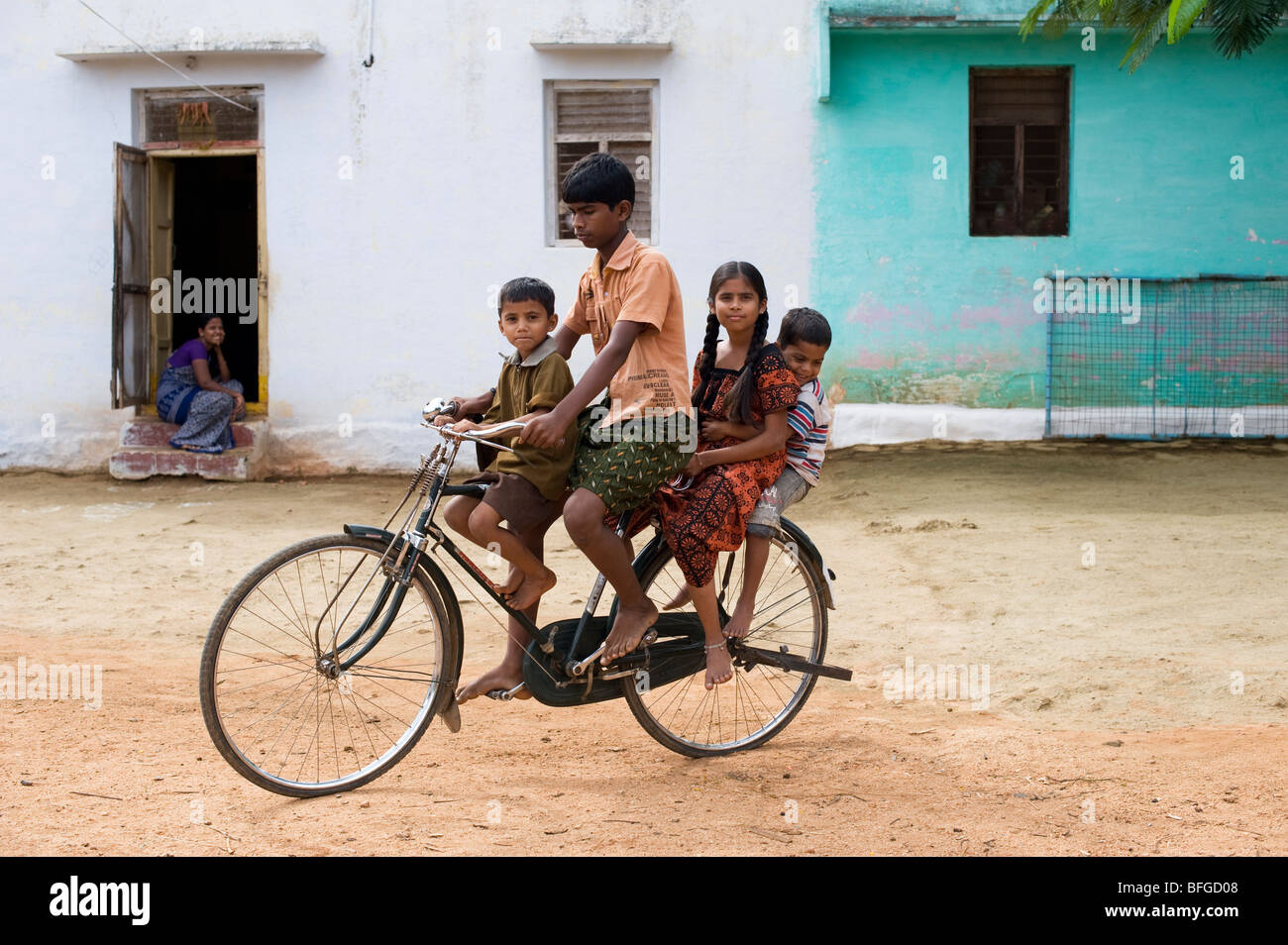 Indian teenager and children riding a bicycle in a rural Indian village ...