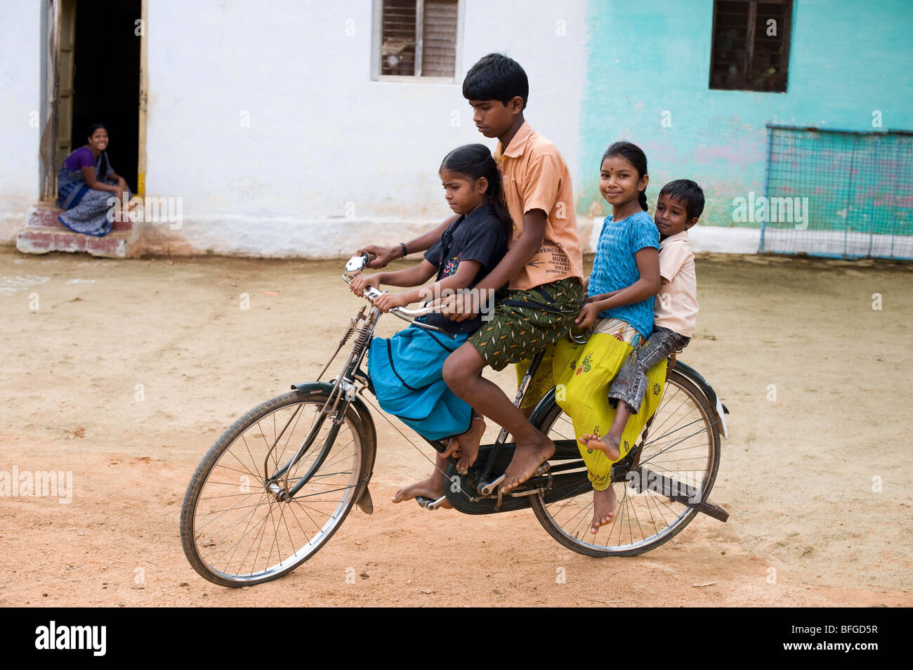 Indian teenager and children riding a bicycle in a rural Indian village ...