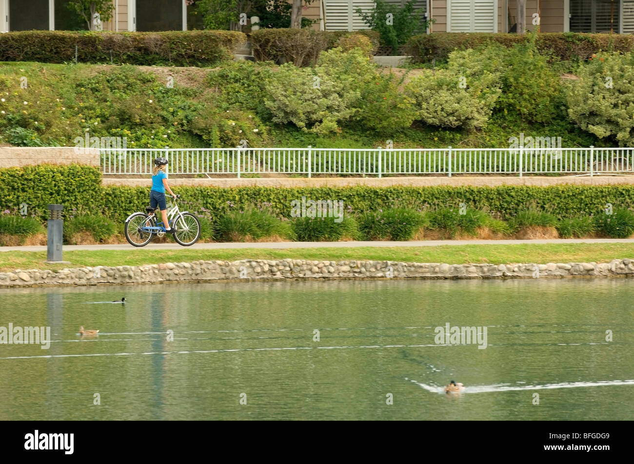 Young girl rides a bicycle along a lakeside path within an upscale ...