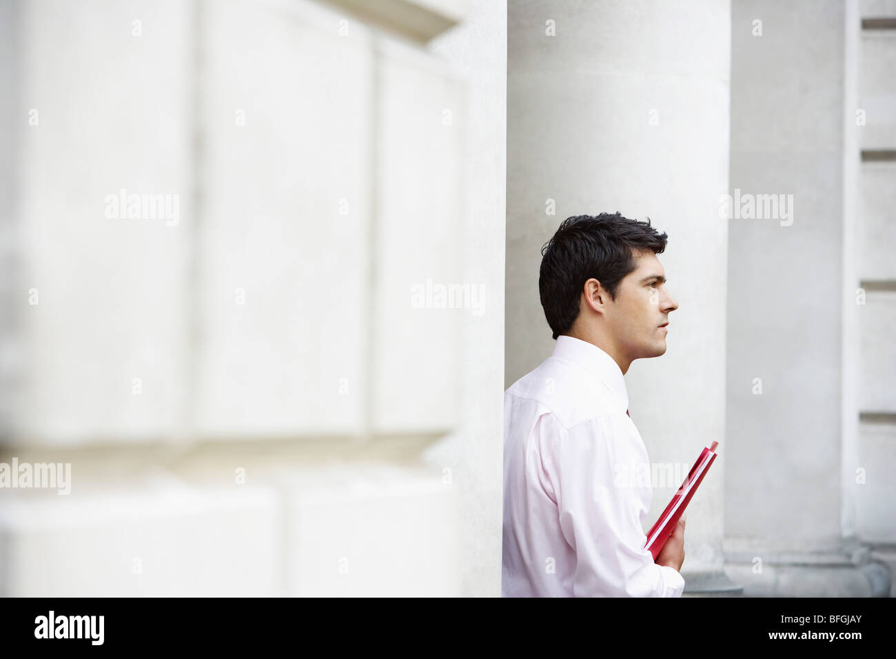 Businessman sitting on pillar outside building holding files Stock ...
