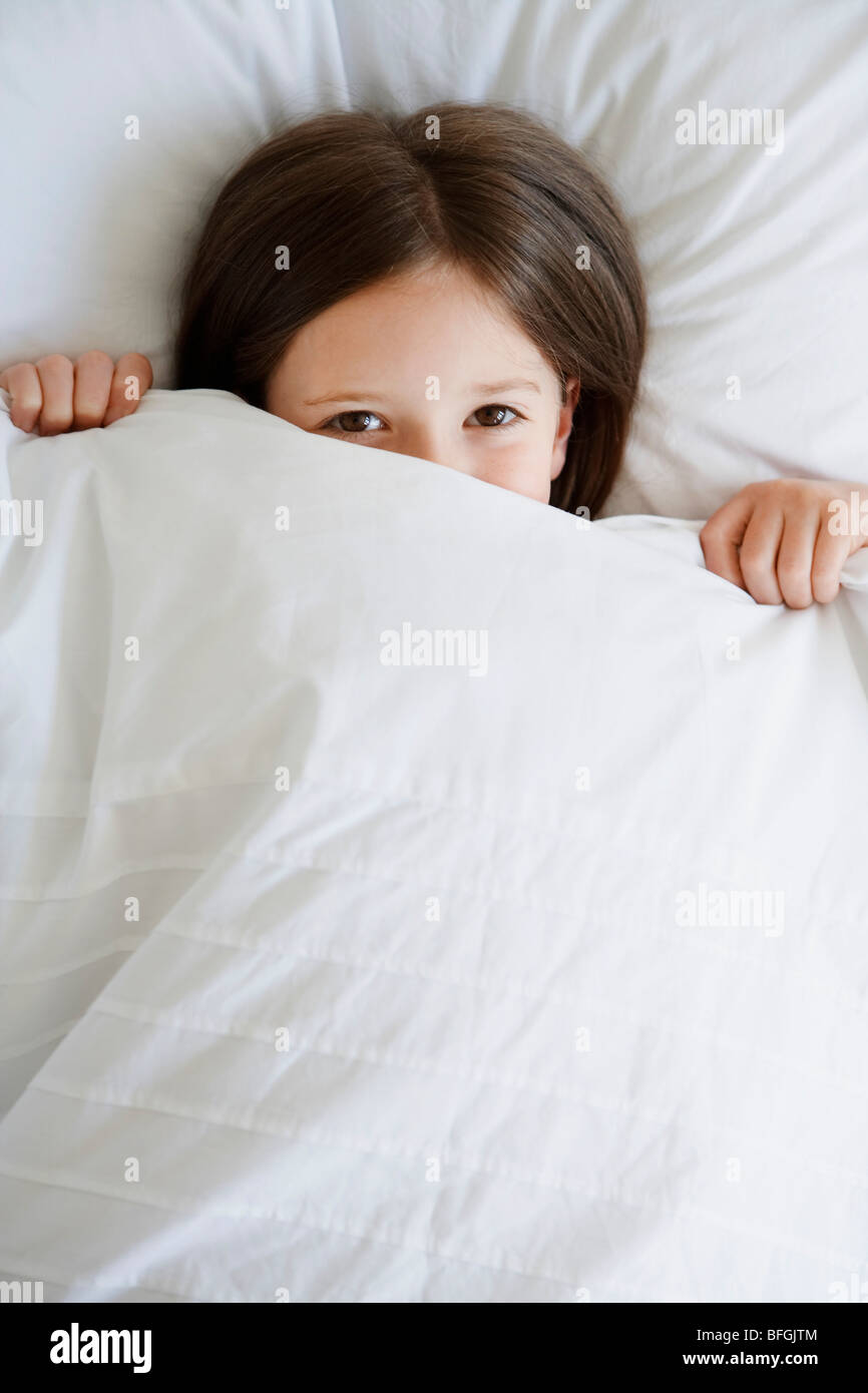 Little girl in bed pulling covers over face, portrait, high angle view ...