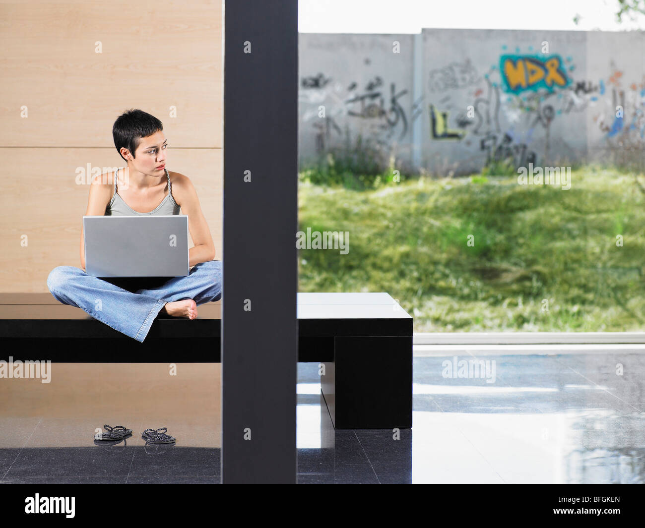 Young woman sitting down using laptop indoors Stock Photo - Alamy