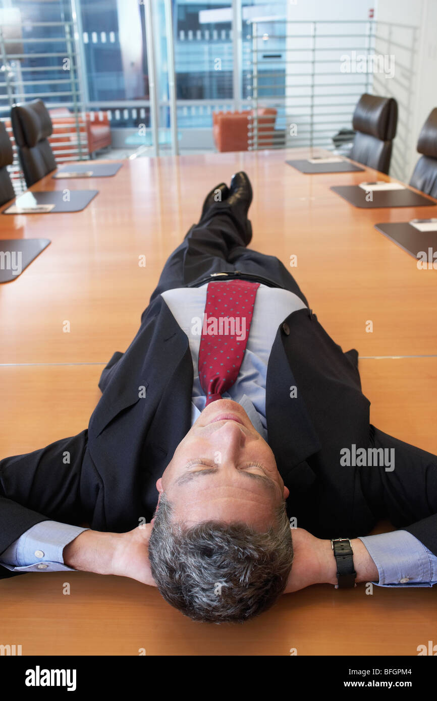 Businessman lying on conference table Stock Photo - Alamy