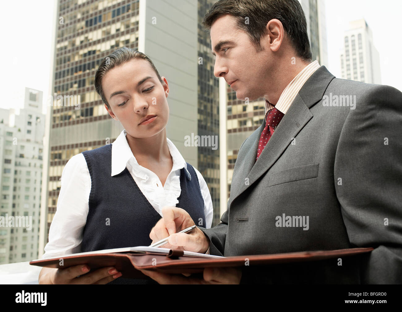 Business man showing paperwork to business woman, outdoors in city ...