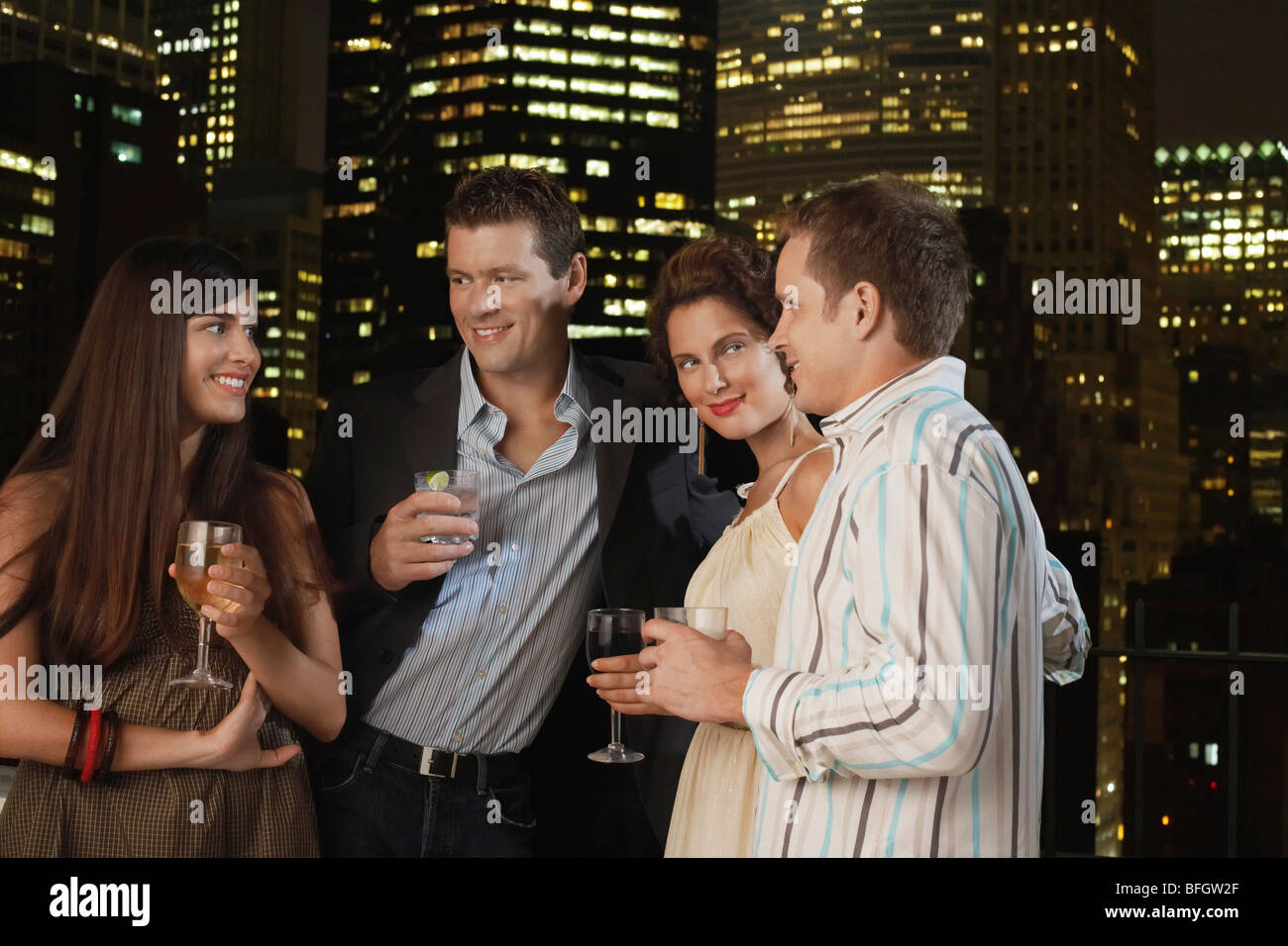 Two couples drinking together against night city skyline Stock Photo ...