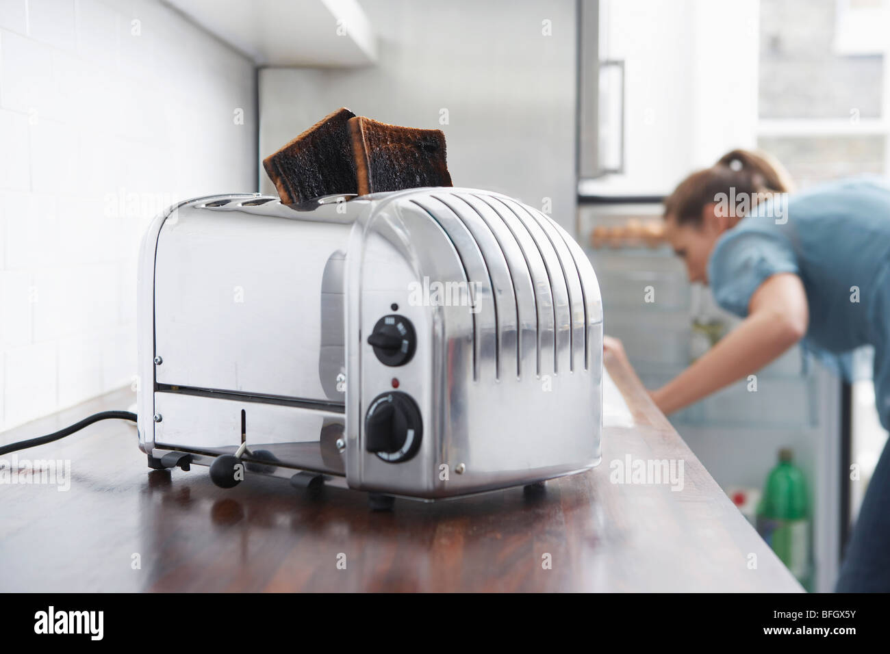 Burned toast in toaster, woman in background Stock Photo - Alamy