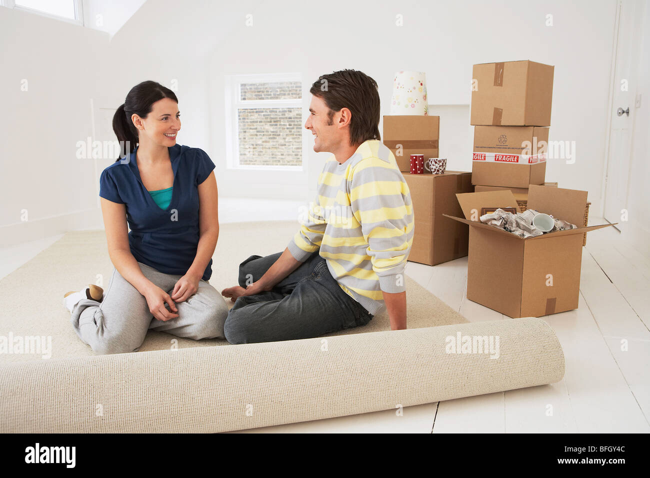 Couple sitting on half-rolled carpet in new home Stock Photo - Alamy