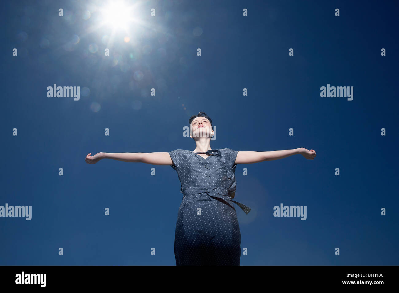 Woman with arms outstretched, standing against sky, low angle view ...