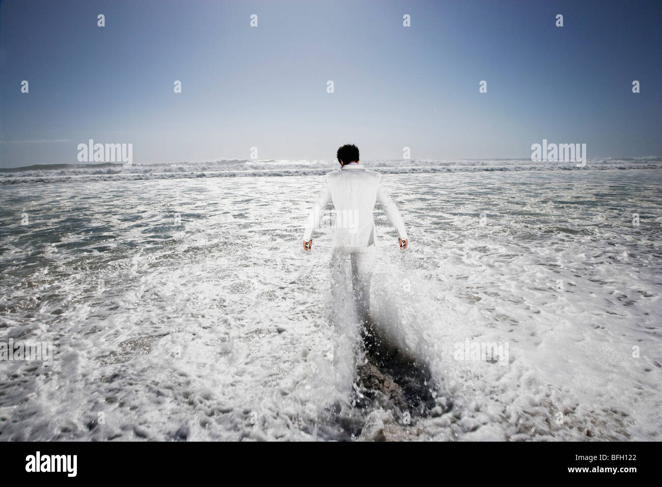 Man walking into sea, being washed by waves, back view Stock Photo - Alamy