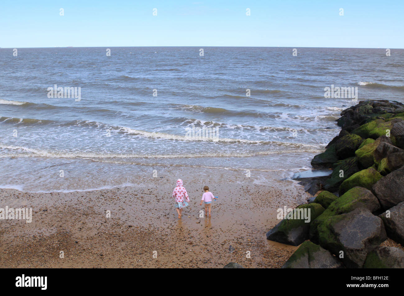 two small children walking towards the sea on a wide spacious beach ...