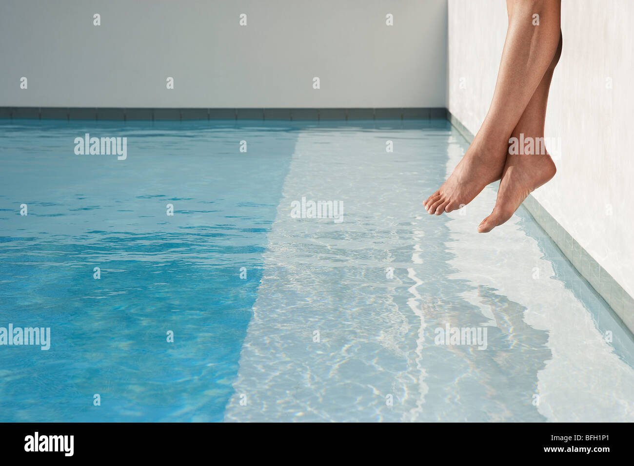 Woman sitting on edge of swimming pool, low section, side view Stock ...