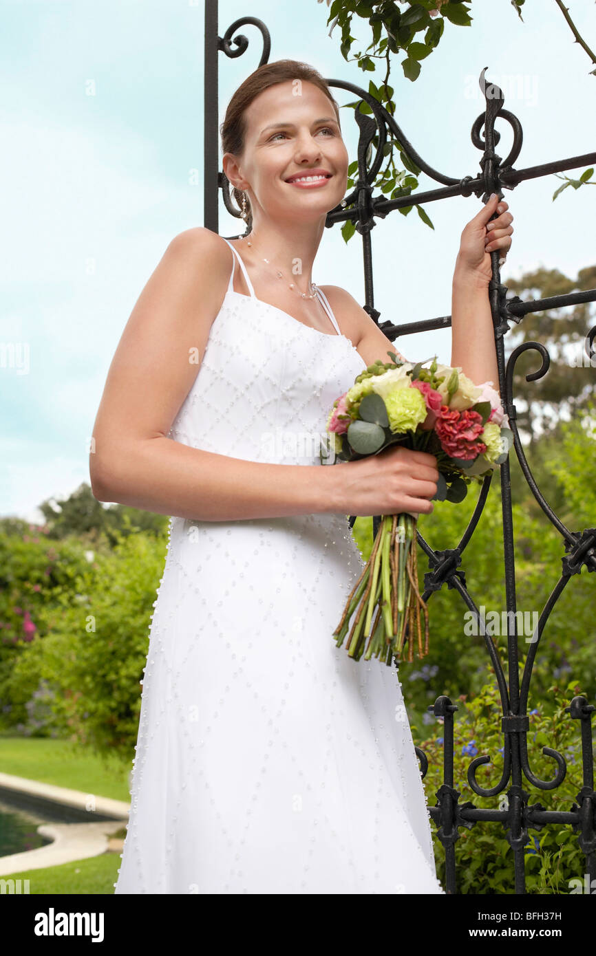 Mid adult bride leaning on gate, holding bouquet, smiling Stock Photo ...