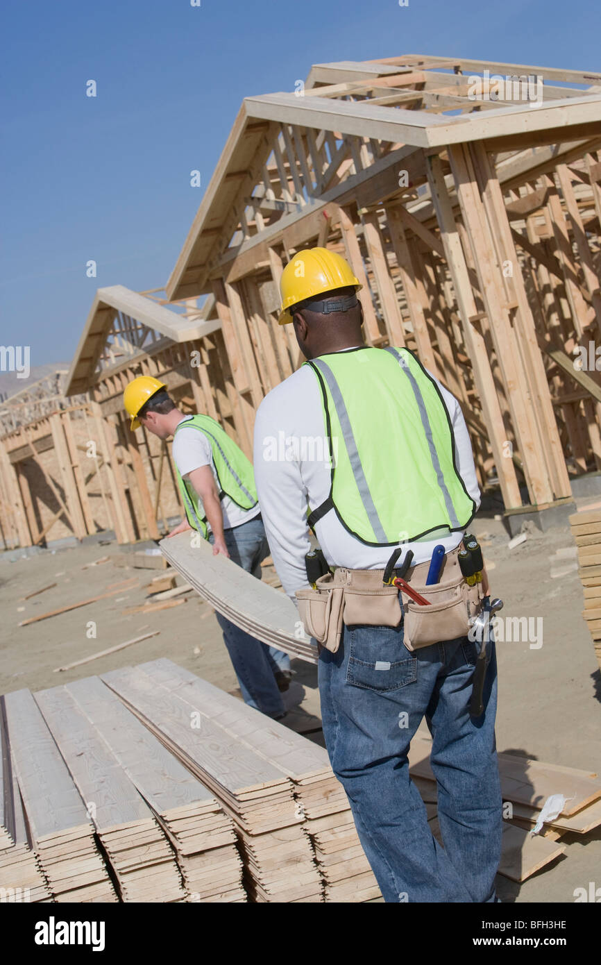 Two construction workers carrying wooden plank on site Stock Photo - Alamy