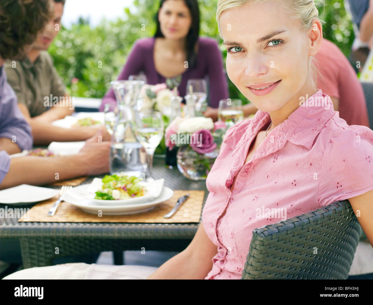 Young woman sitting with friends around patio table, socialising ...
