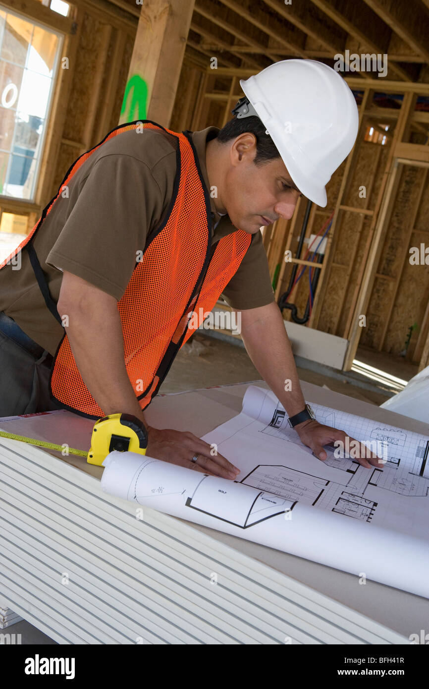 Construction worker examining blueprints inside half constructed house ...