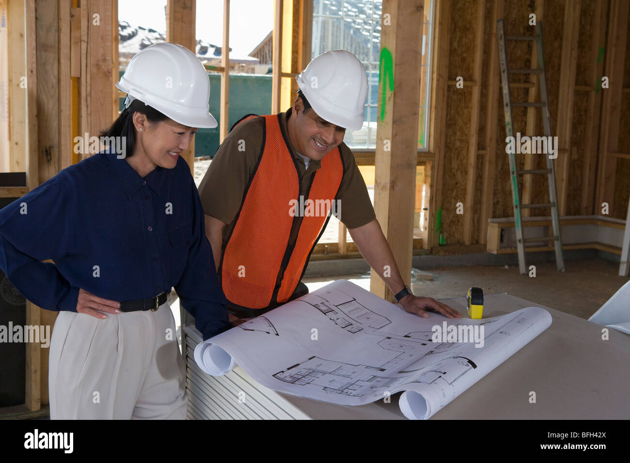 Architect and construction worker looking at blueprints inside half ...