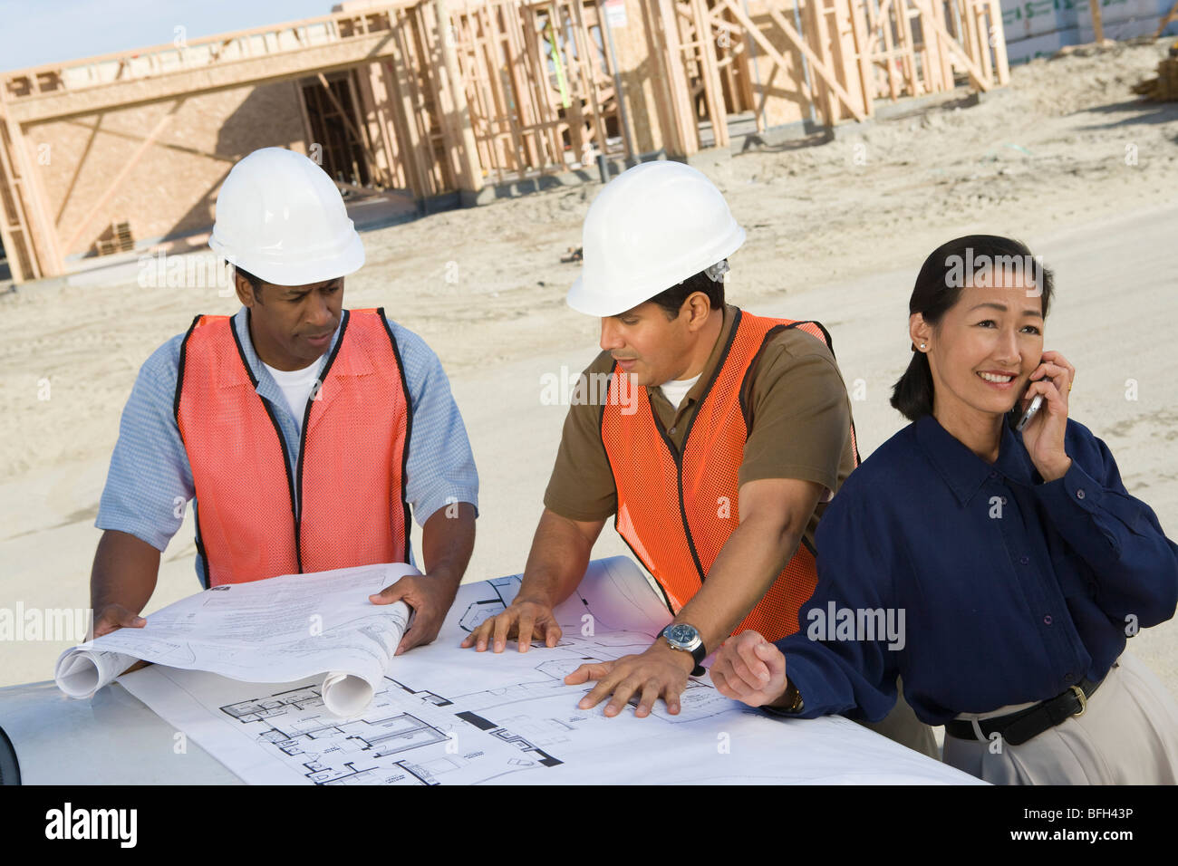 Two construction workers looking at blueprints and architect talking on ...
