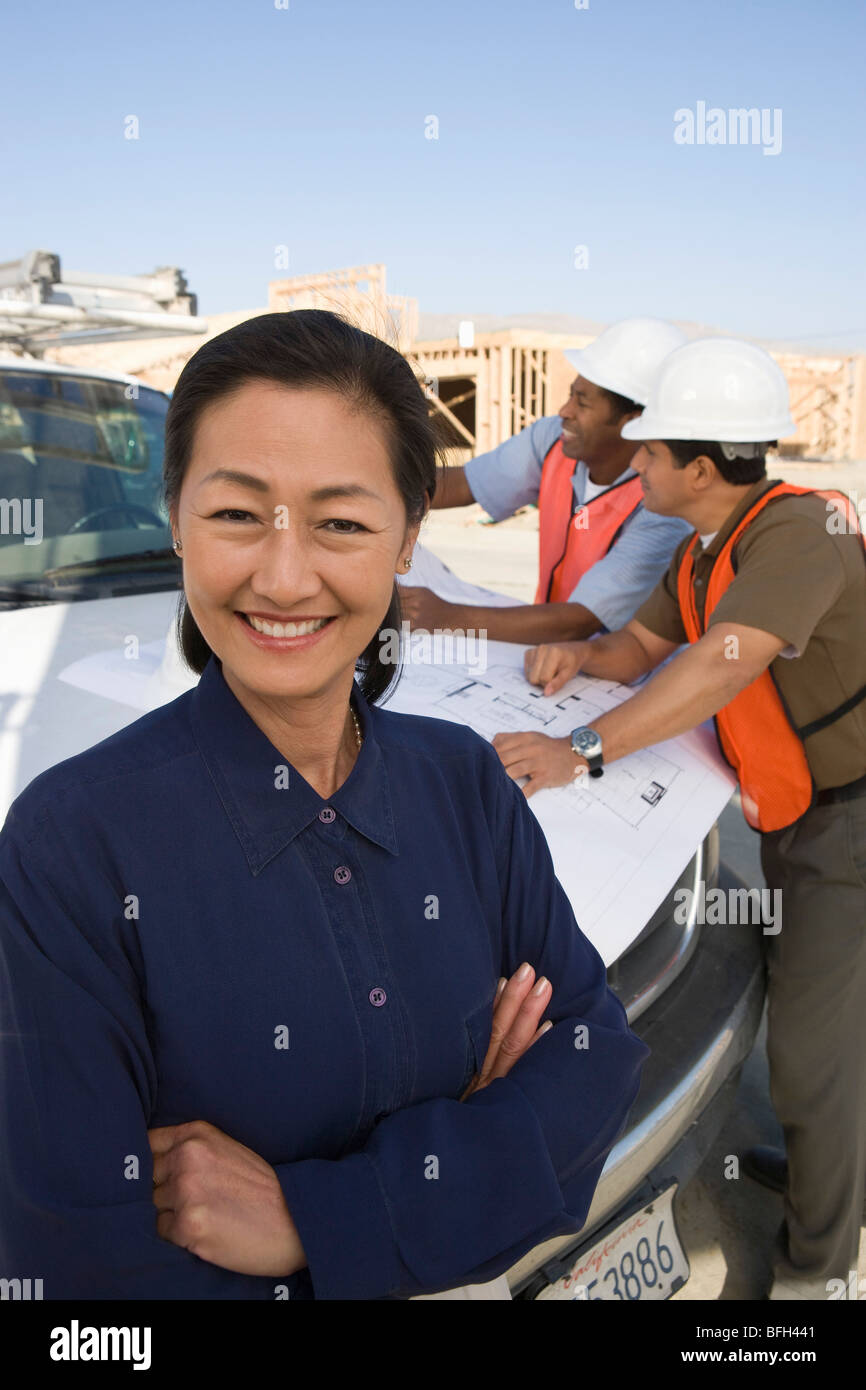 Two construction workers looking at blueprints and architect talking on ...