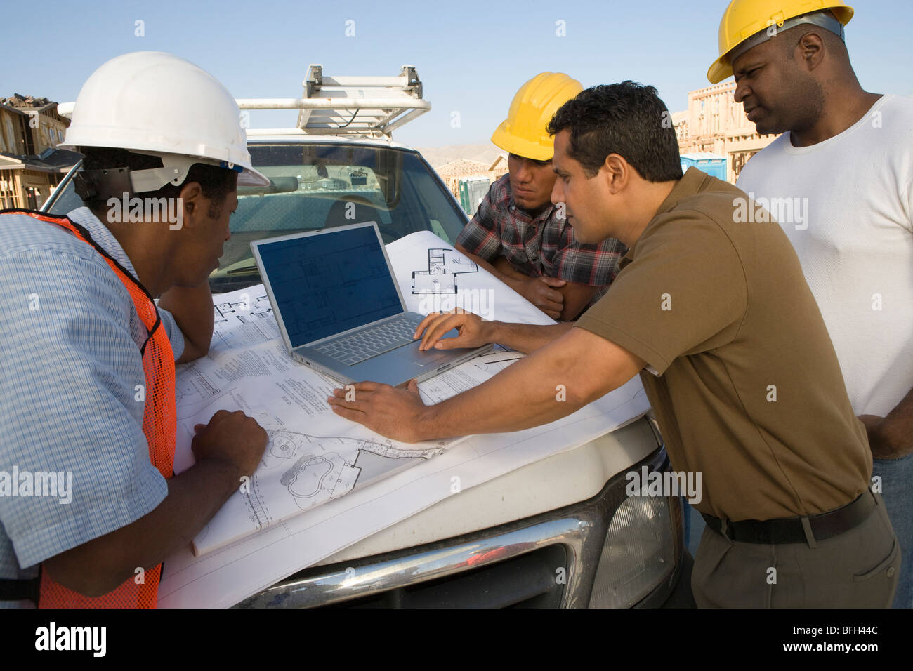 Four construction workers standing in front of car on construction site ...