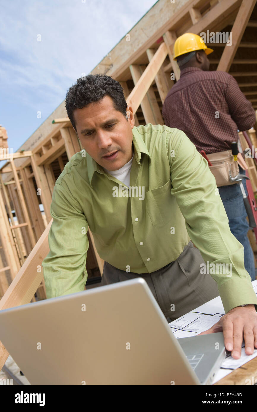 Architect using laptop on construction site with construction worker ...