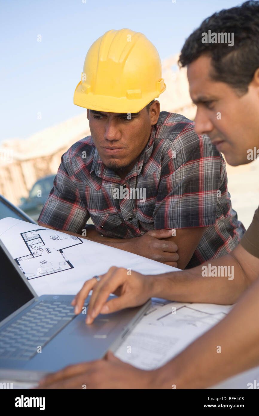 Architect and construction worker using laptop on construction site ...