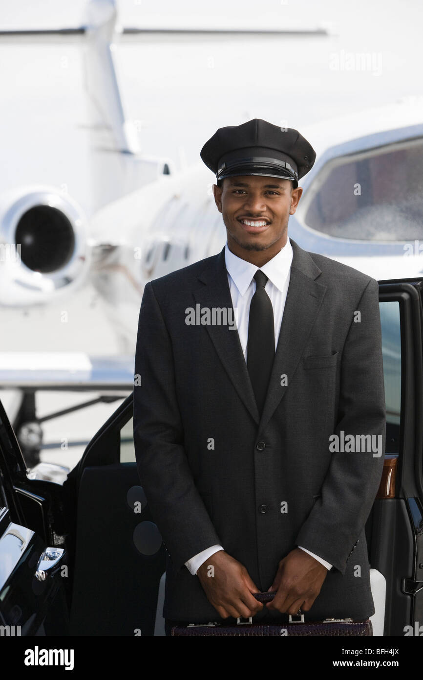Portrait of mid-adult chauffeur standing in front of limousine and ...