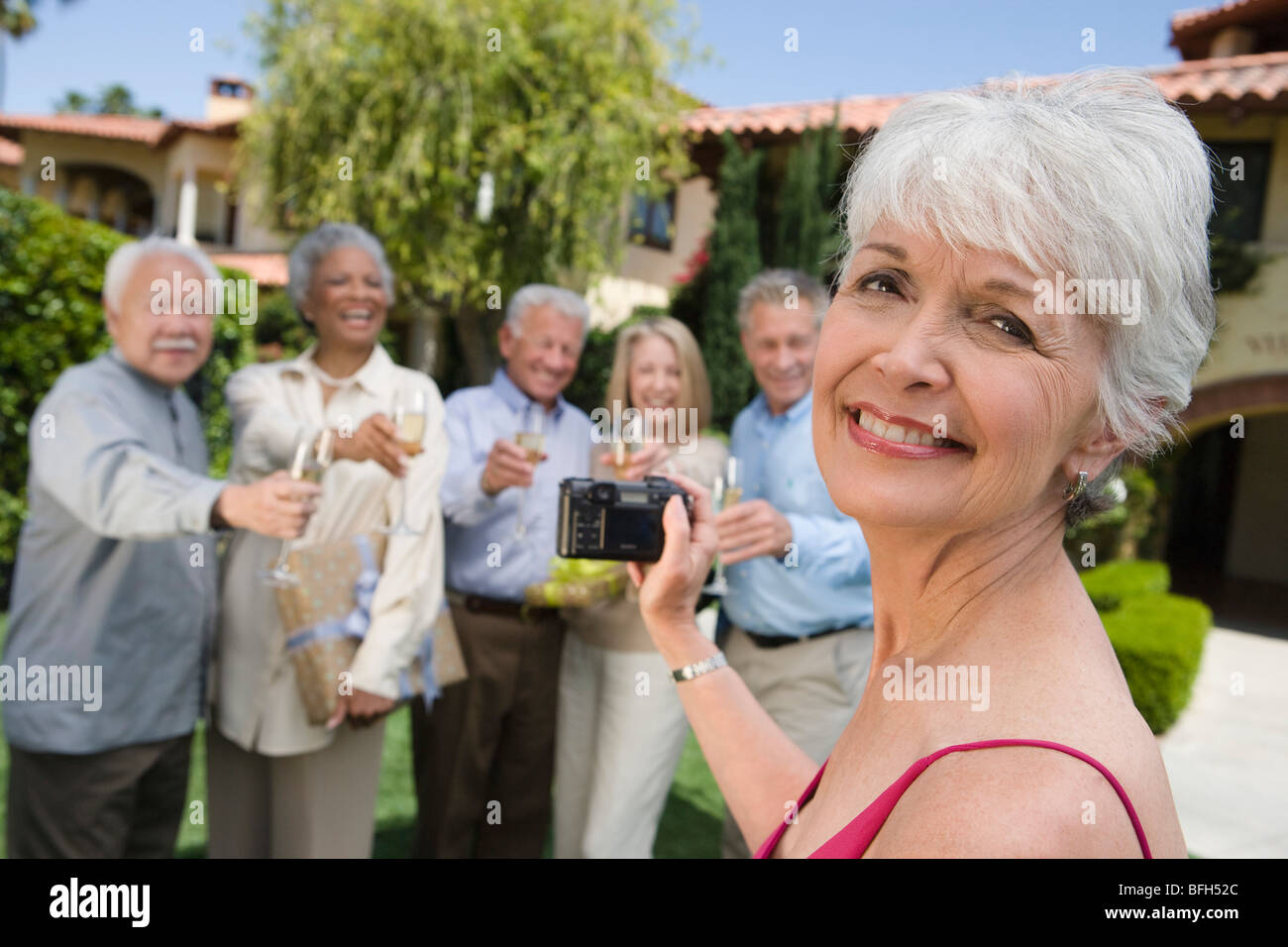 Senior woman photographing friends in garden while raising toast Stock ...