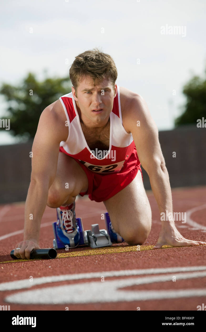 Young man in starting blocks holding relay baton, portrait Stock Photo - Alamy