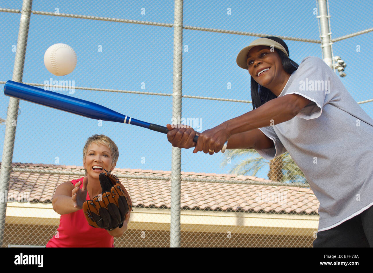 Senior woman hitting softball with other woman catching Stock Photo - Alamy