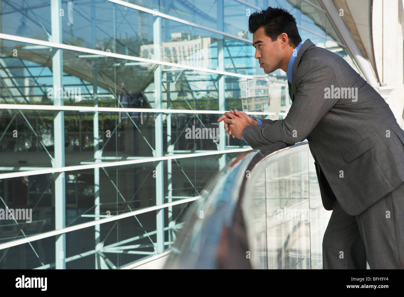 Businessman leaning on railing outside office building Stock Photo - Alamy