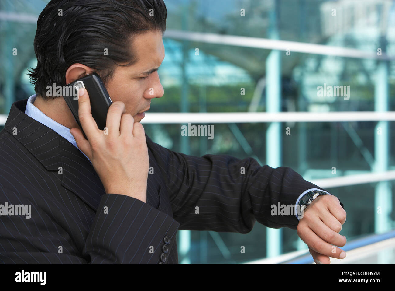 Businessman using mobile phone and checking watch outside office ...