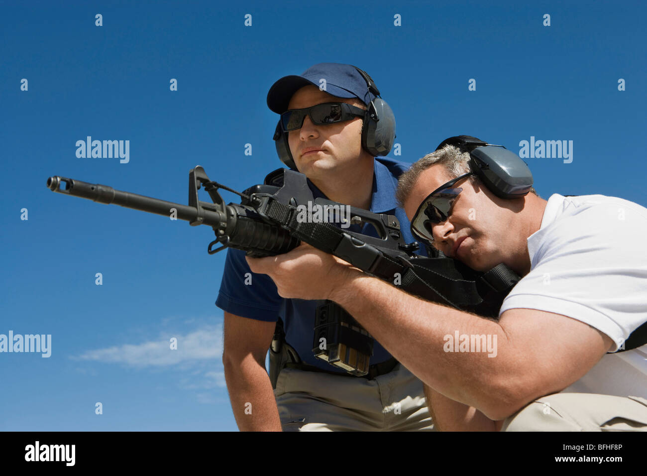Instructor with man aiming machine gun at firing range, low angle view ...