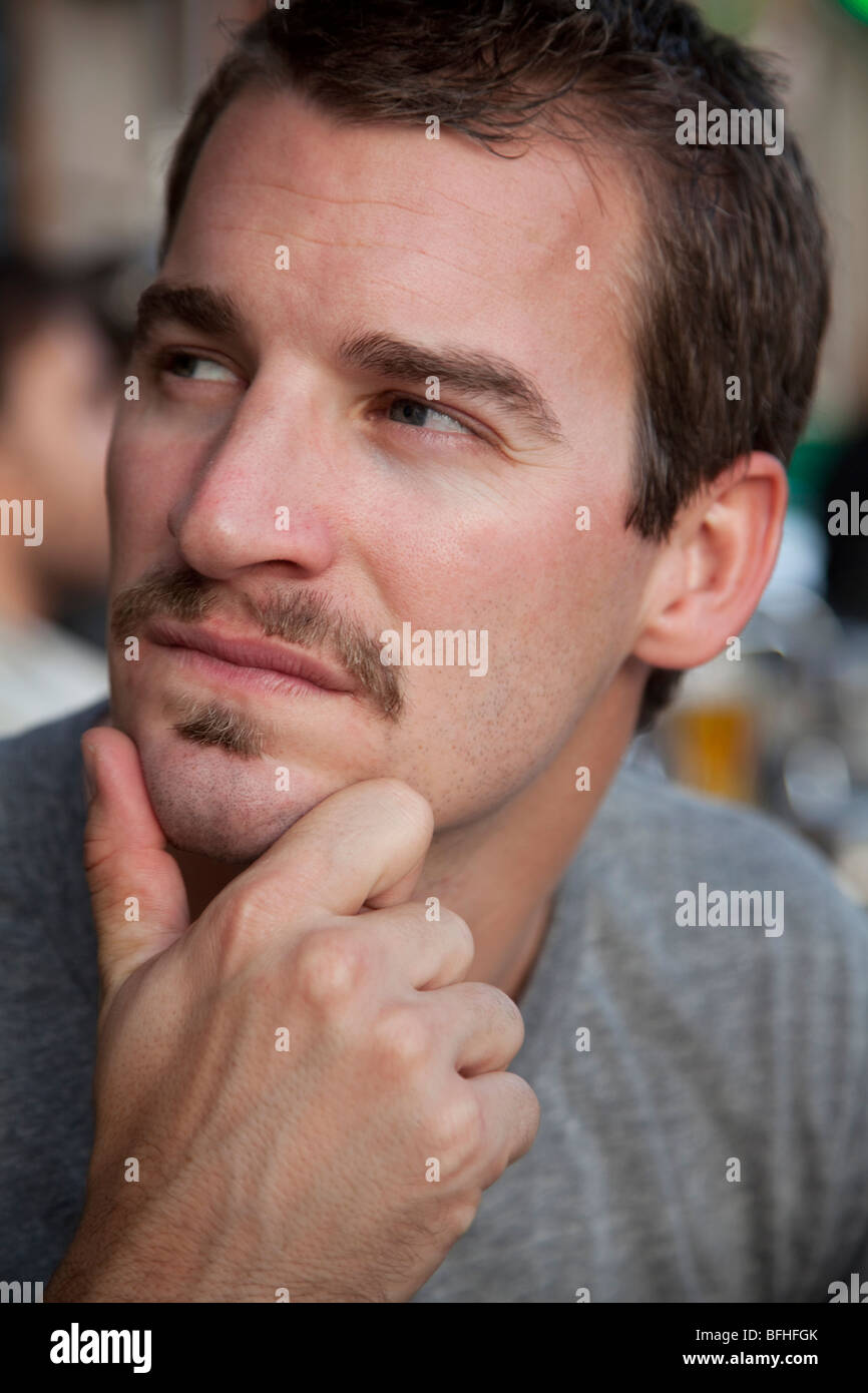 portrait of a young man holding chin and thinking Stock Photo - Alamy