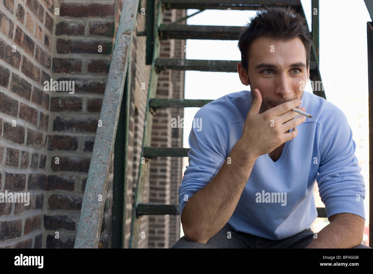 Young Man Smoking on Fire Escape Stock Photo - Alamy