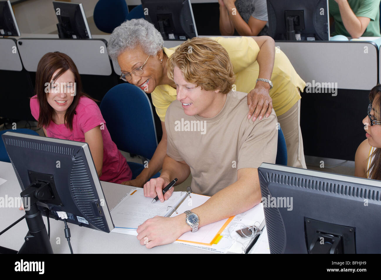 Teacher helping two students working in computer classroom Stock Photo ...