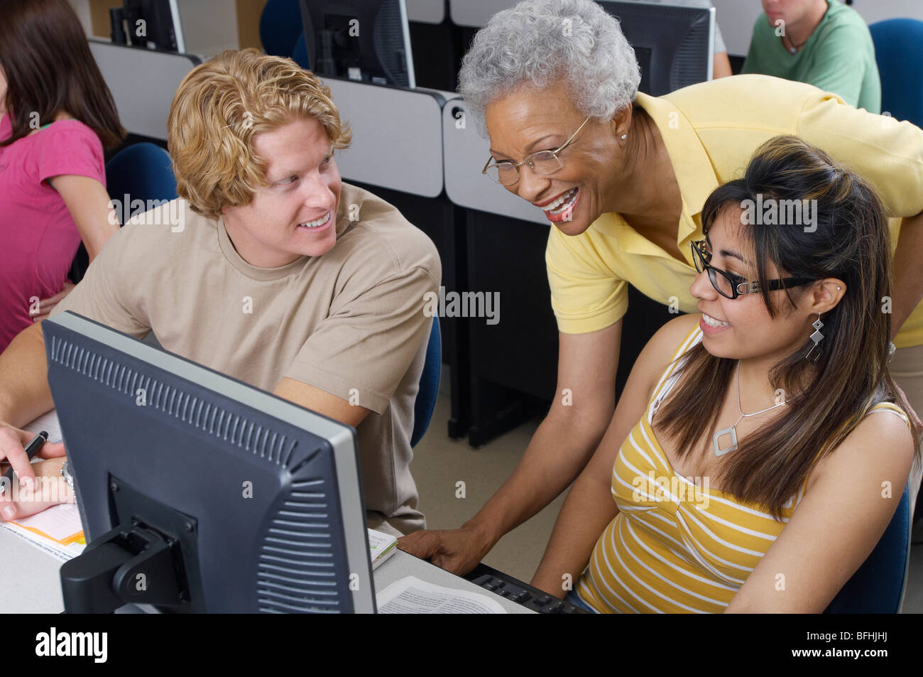 Teacher helping two students working in computer classroom Stock Photo ...