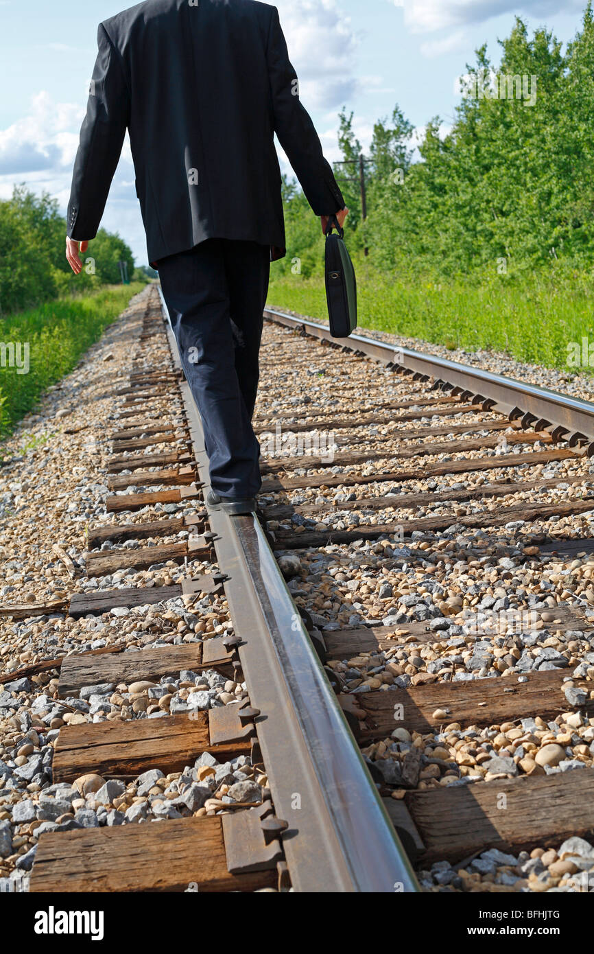 Middle age businessman walking on rail road line with briefcase in hand ...