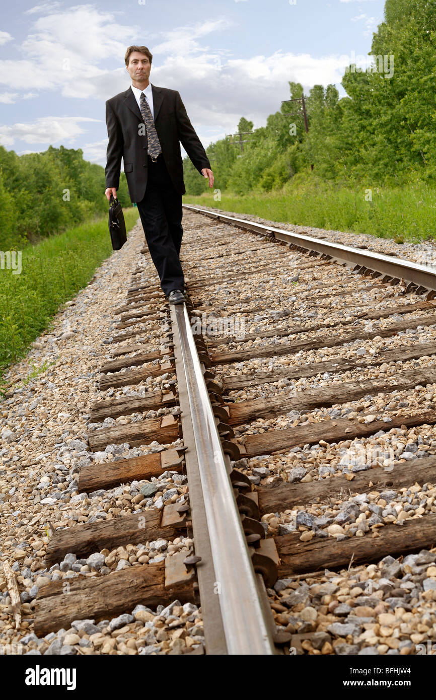 Middle age businessman walking on rail road line with briefcase in hand ...