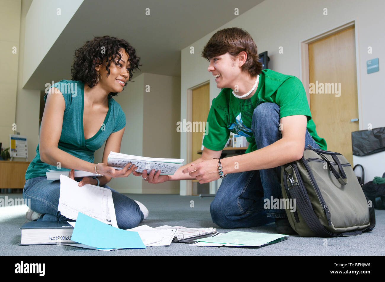 Male student assisting female student, picking up books from floor ...