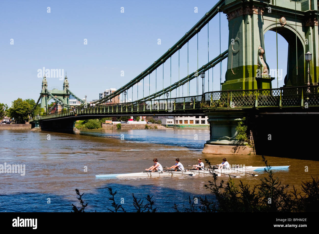 Young boys practice rowing in a four man team past Hammersmith Bridge ...
