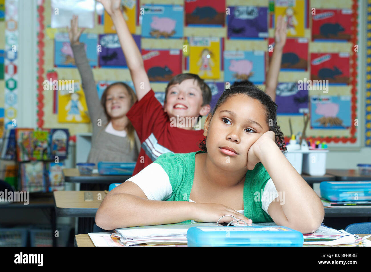 Three pupils in classroom, two with raised hands, one pensive Stock ...
