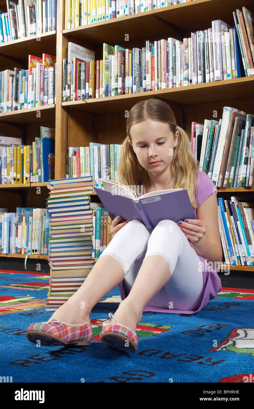 Girl sitting on the floor and reading book in library Stock Photo - Alamy