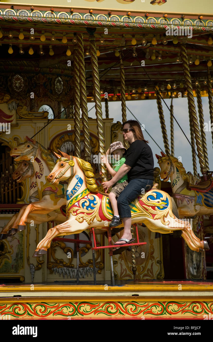 mother and young boy riding together on steam galloper fairground ...