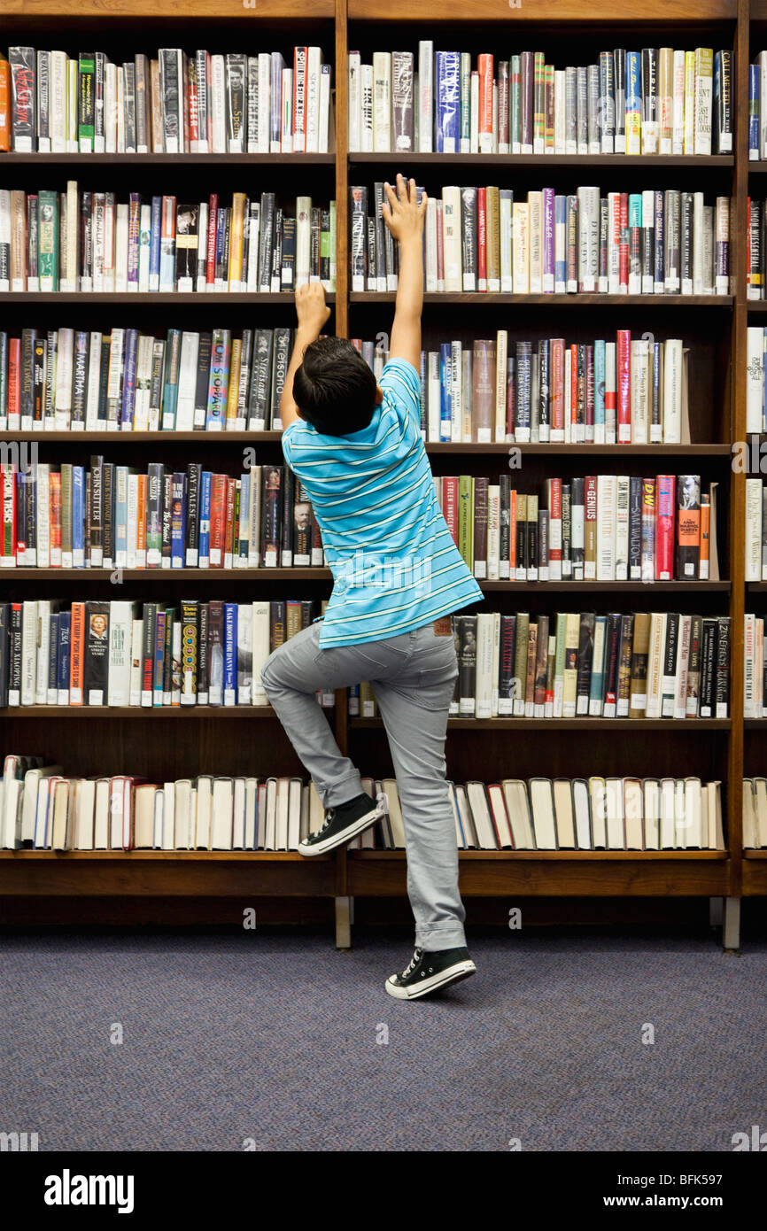 Boy reaching for book on library shelf Stock Photo - Alamy