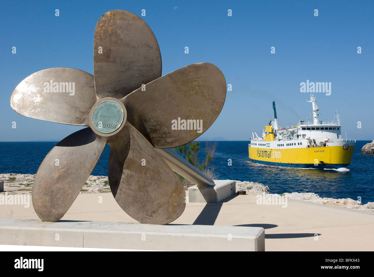 A yellow ferry entering Ciutedella Harbour set against a ship's ...